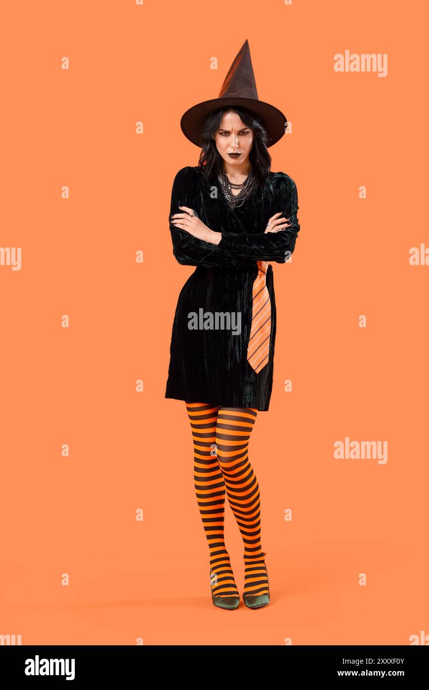 Beautiful young angry woman dressed as witch for Halloween on orange ...