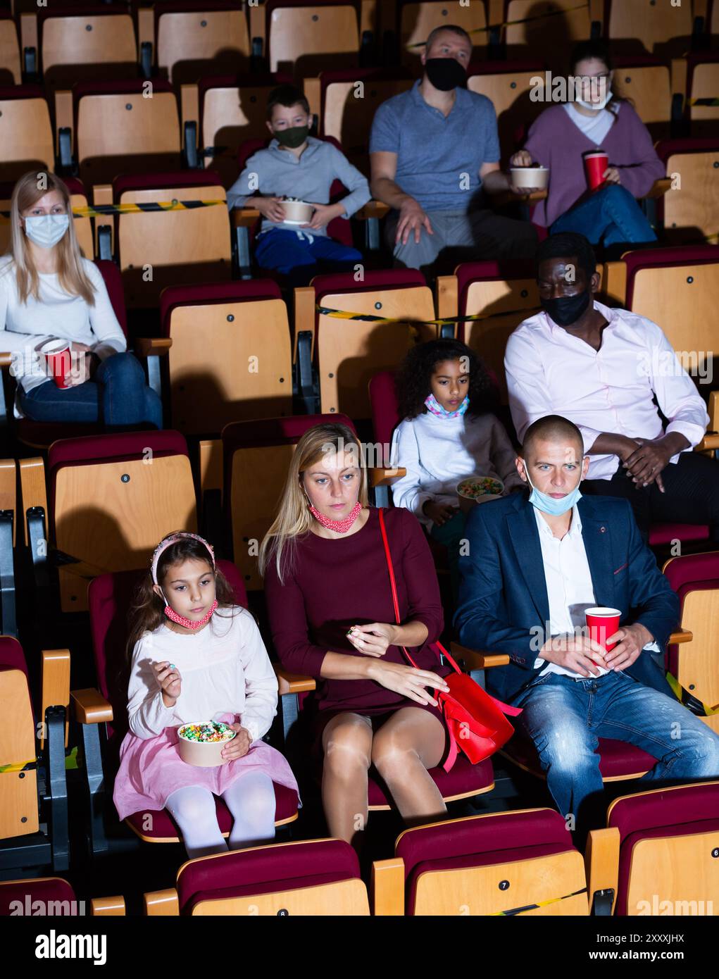Adults with children in protective masks watching movie in cinema Stock ...