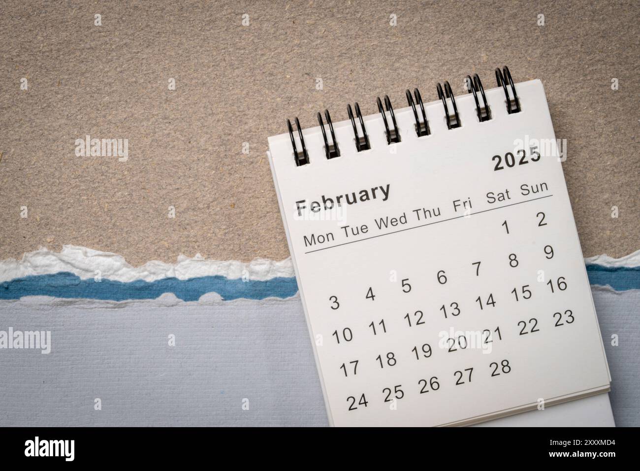 February 2025 - small spiral desktop calendar against abstract paper ...