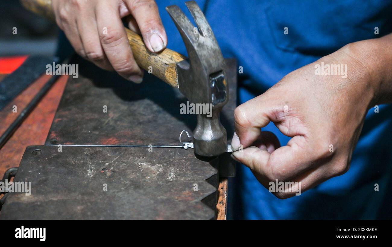 Goldsmith shaping a silver wire with hammer on an anvil in his workshop ...