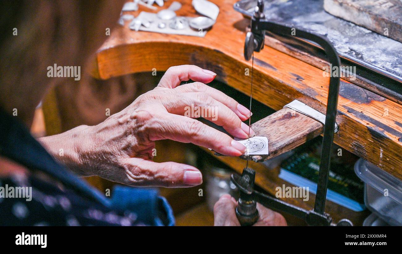 Goldsmith is carefully cutting a silver plate with a jeweler saw in a ...