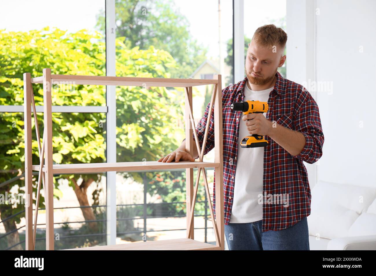 Man with electric screwdriver assembling wooden shelving unit at home ...