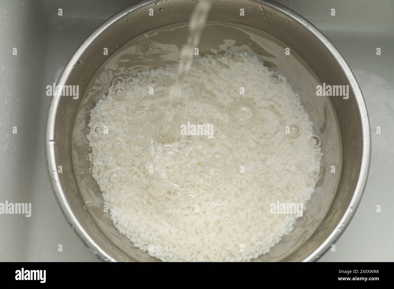 Pouring water into bowl with rice in sink, top view Stock Photo - Alamy