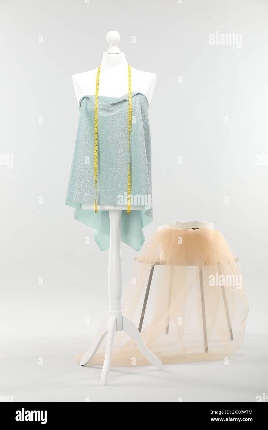 Mannequin with measuring tape, fabric and box on side table against ...