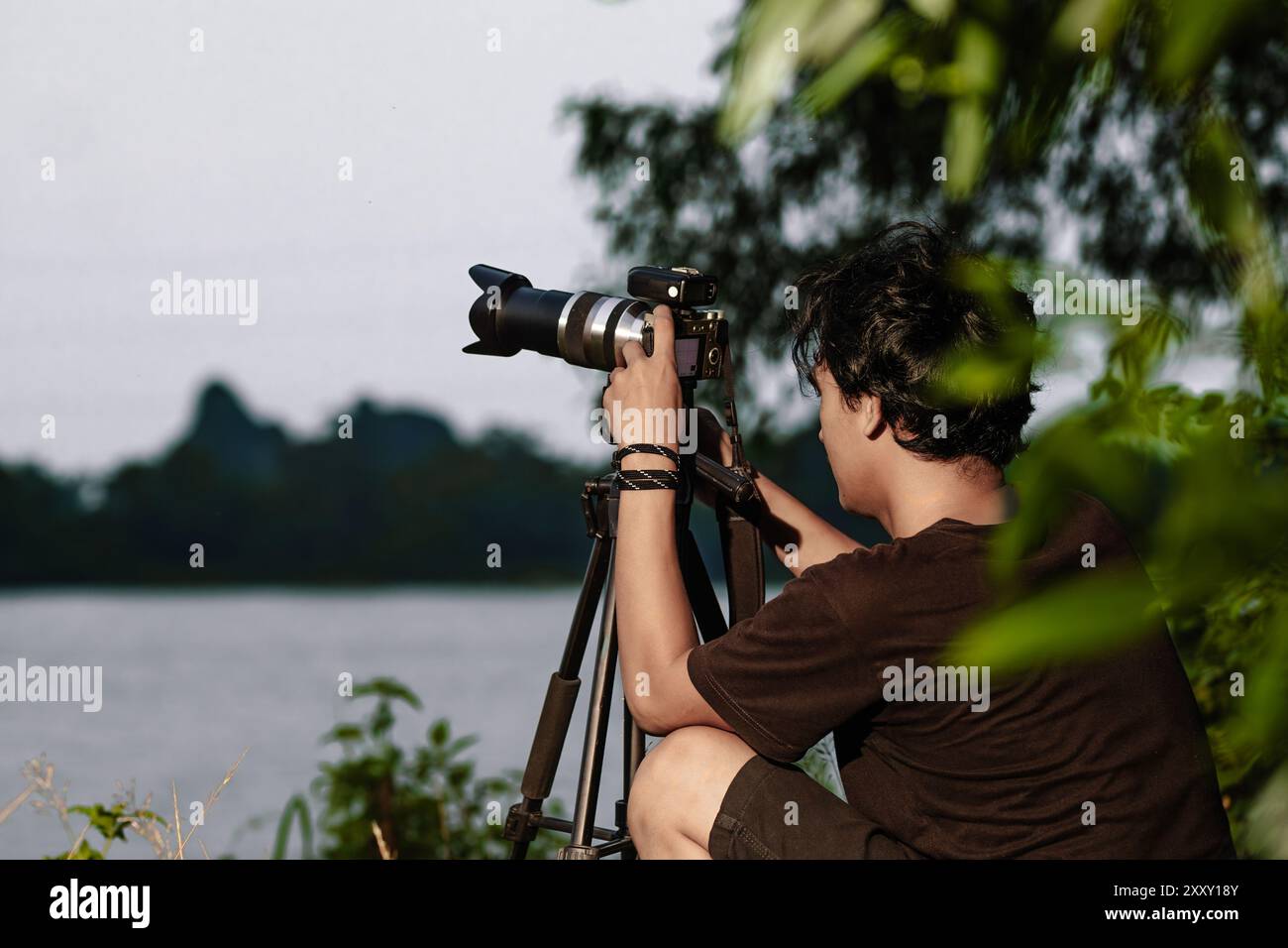 Young man setting up camera on the edge of the lake. Back view of man ...