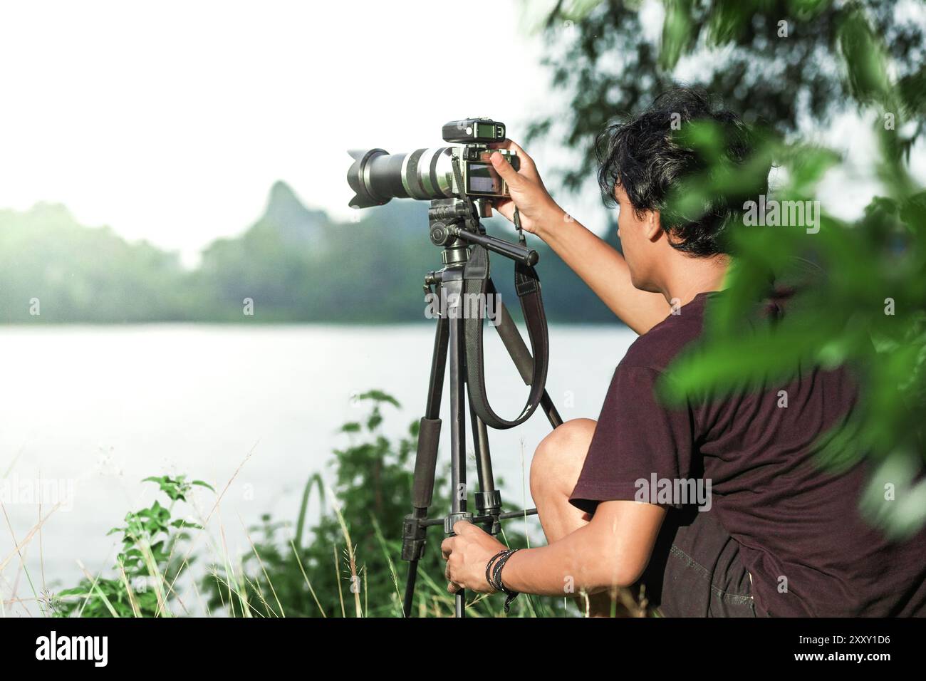 Young man setting their camera with tripod beside the lake. Young man ...