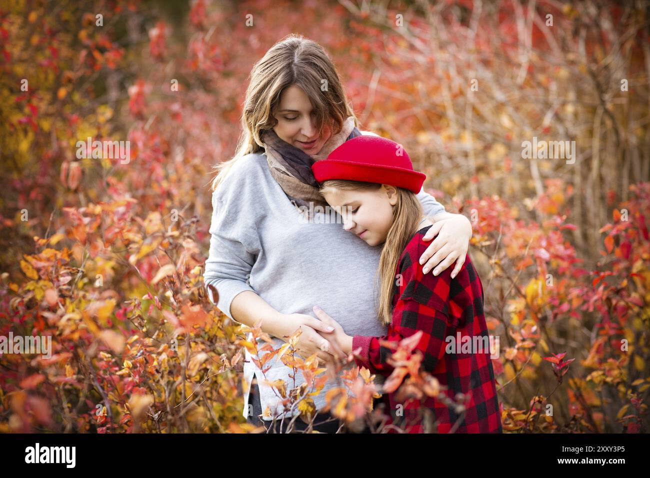 Happy young pregnant mother hugging with teen daughter in autumn park ...