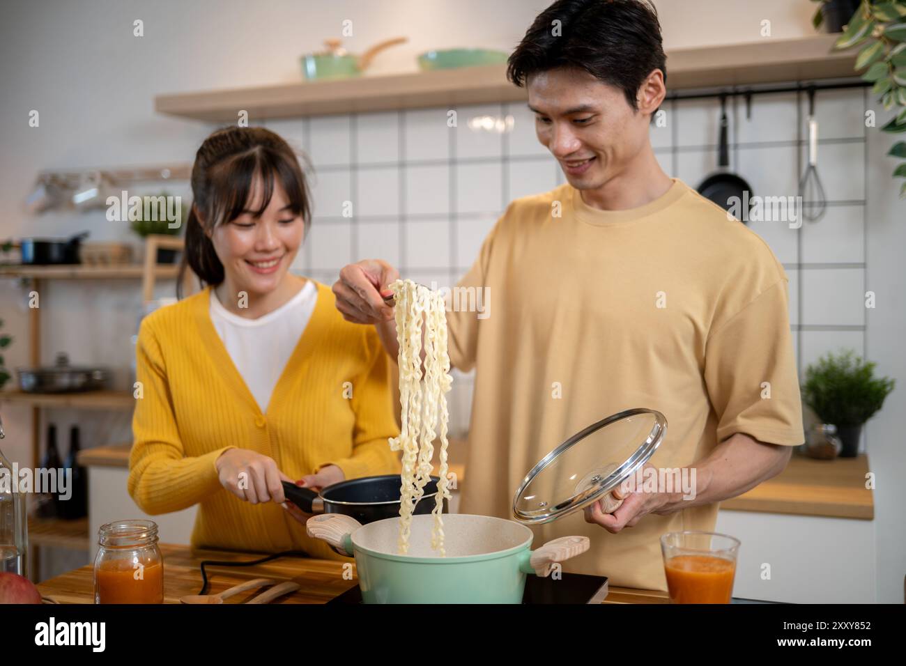 A lovely young Asian couple is enjoying making noodles together in the ...
