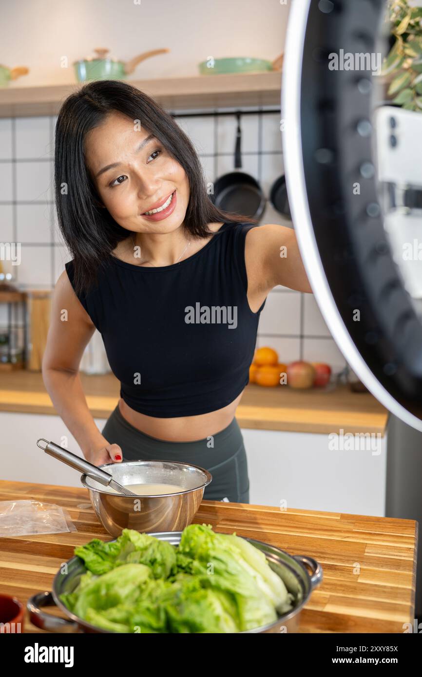 A beautiful Asian female food blogger or influencer is recording ...