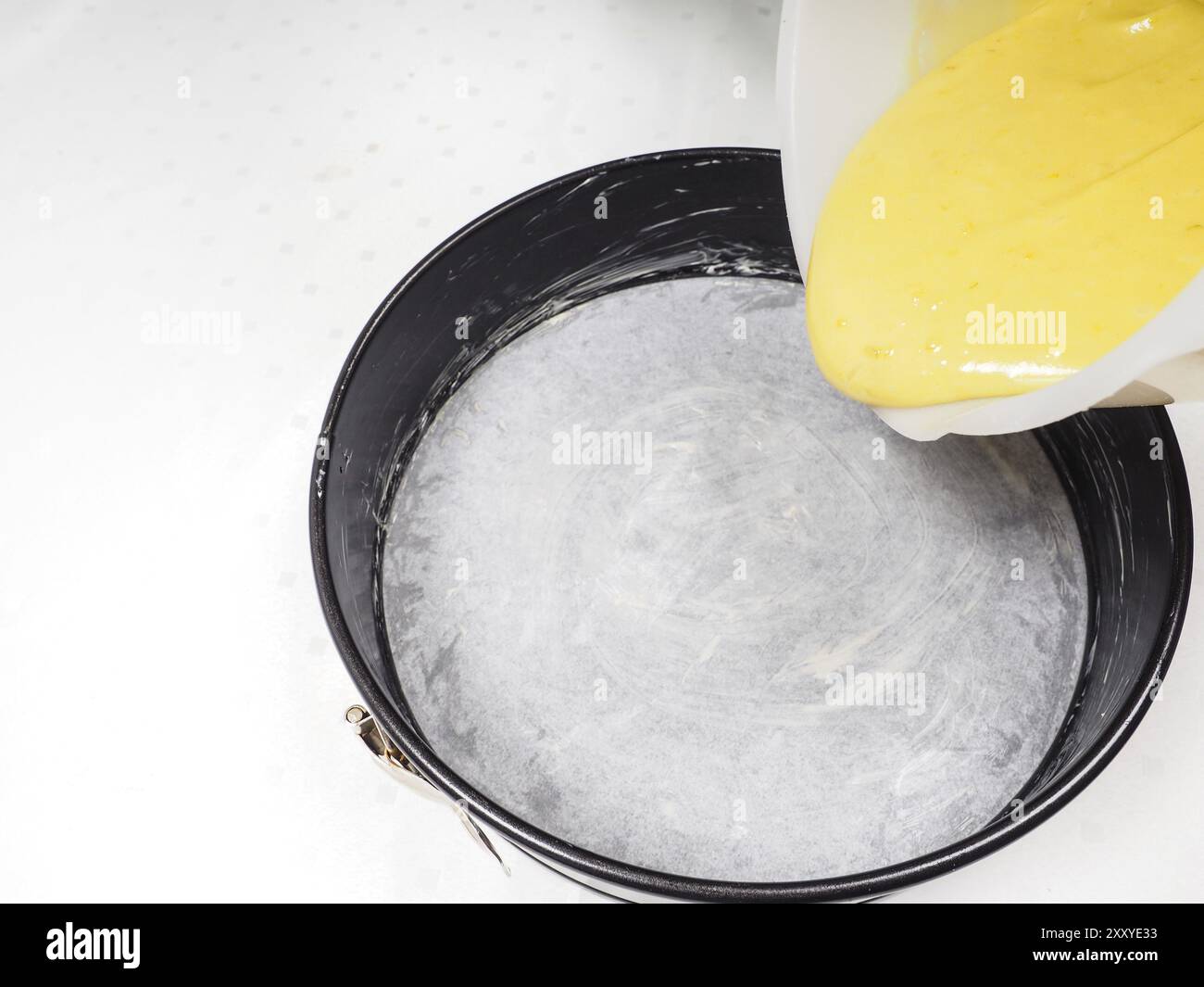 Adding cake mixture from white plastic bowl into a cake shape with ...