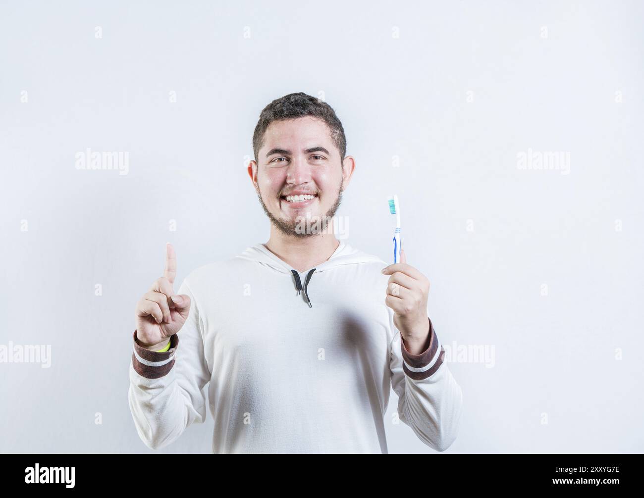 Positive young man holding toothbrush pointing up. Happy guy holding ...