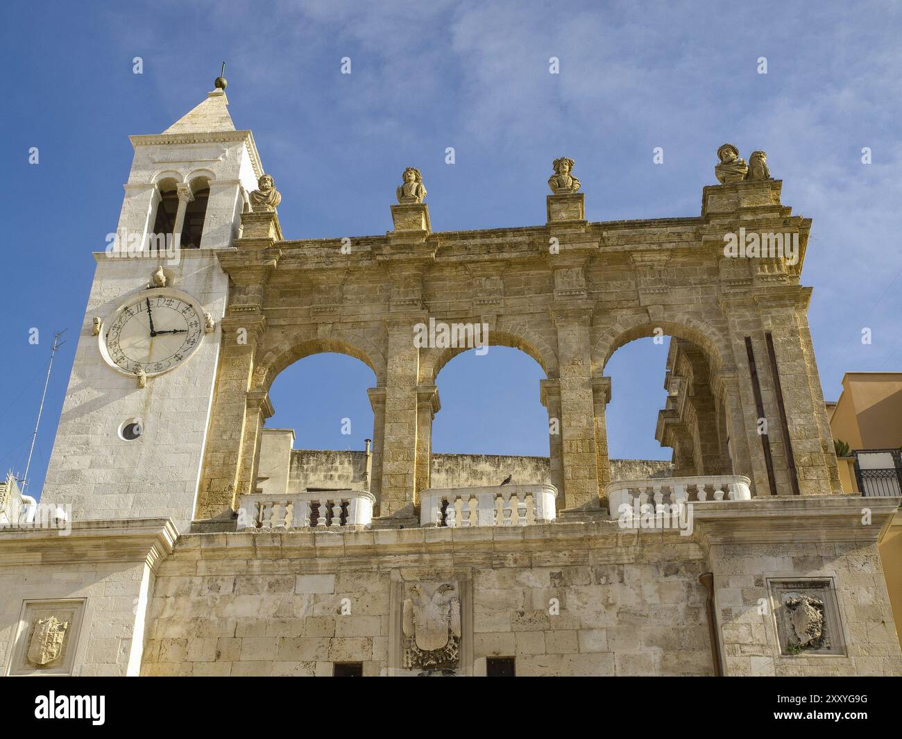 A historic clock tower with arches and sandstone statues under a clear ...