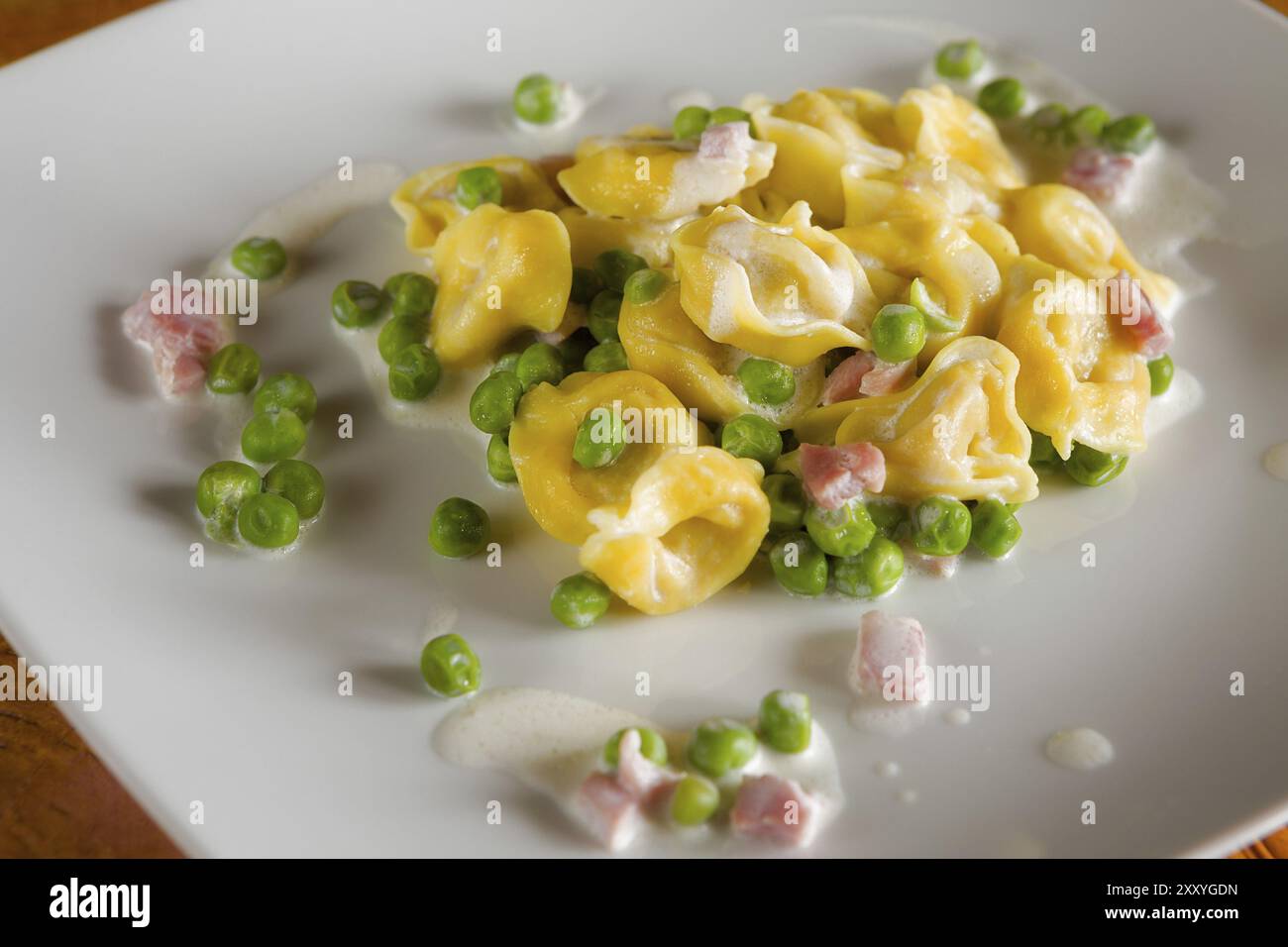 Tortellini with cream ham and peas on a white square plate Stock Photo ...