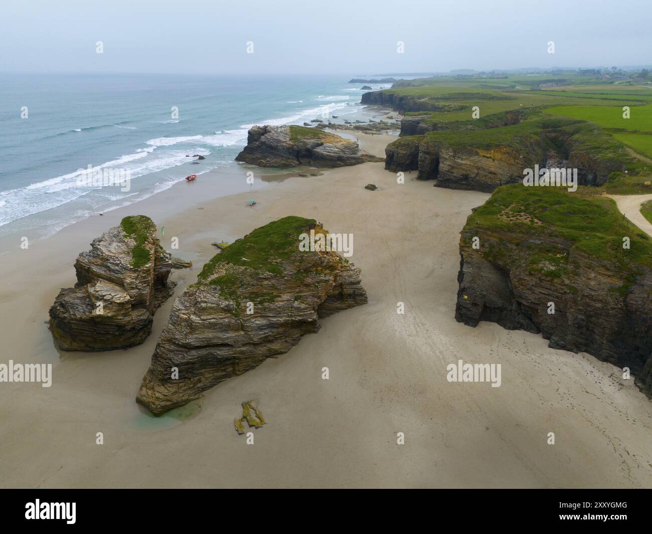 Wide beach with scattered large rock formations and calm water ...