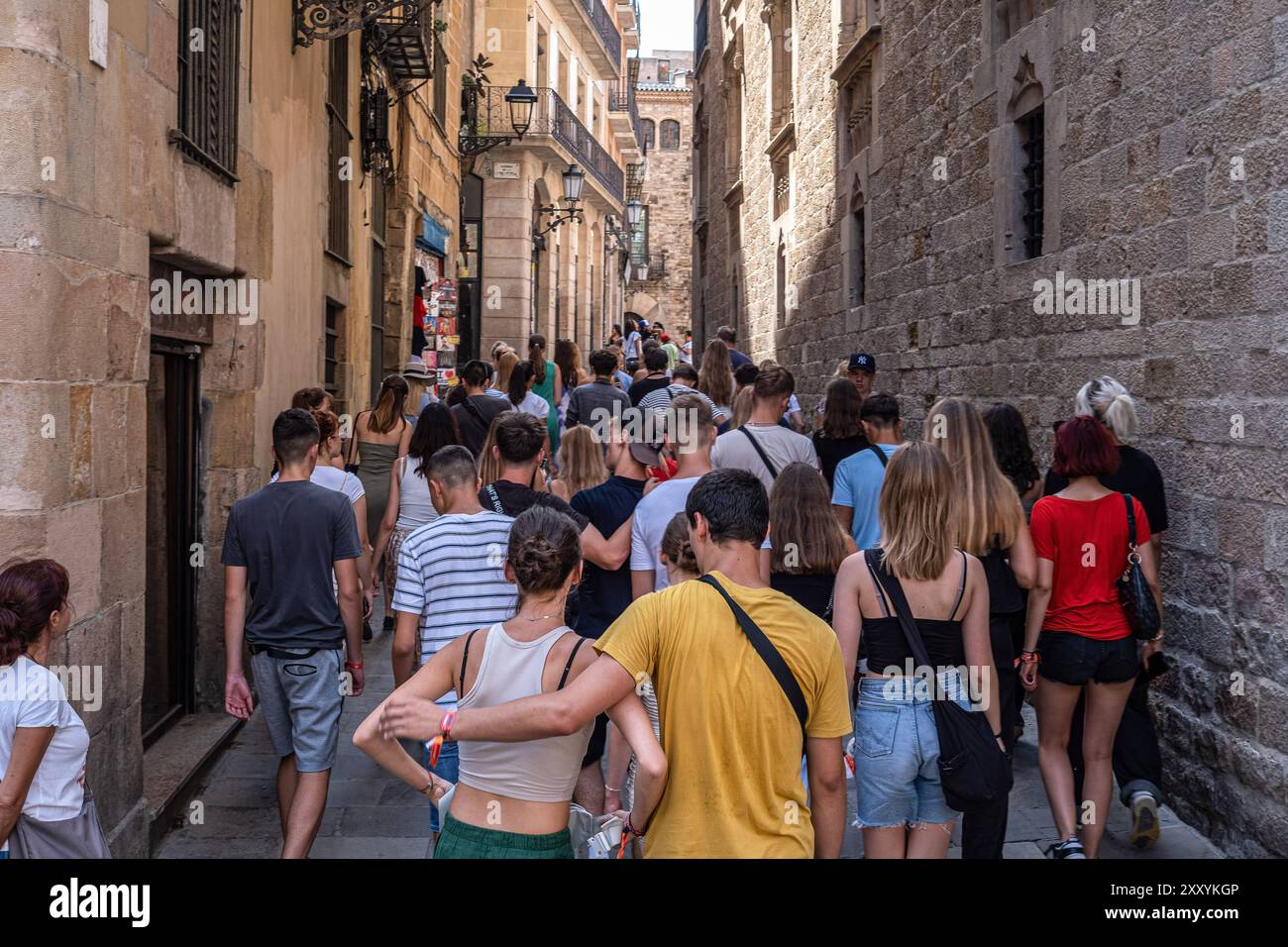 A large group of tourists are seen walking along a narrow street ...