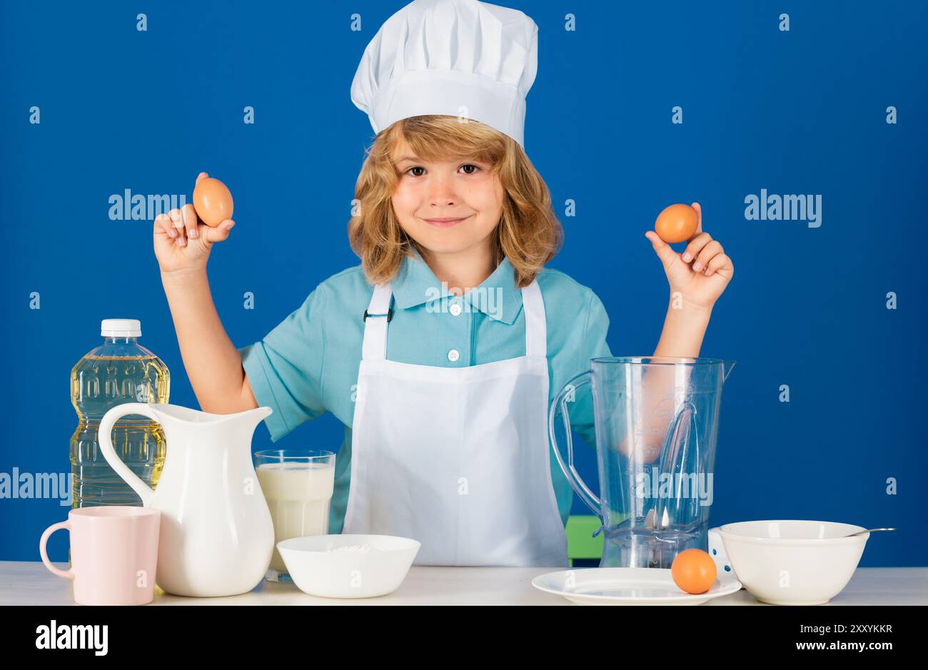Child chef cook hold eggs prepares food in isolated blue studio ...