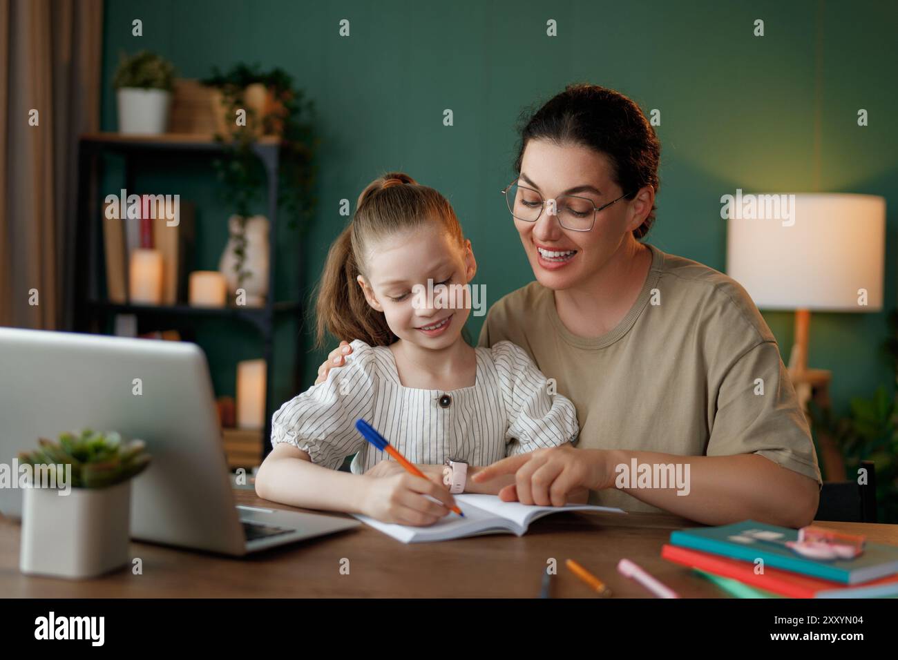 Happy child and adult are sitting at desk. Girl doing homework or ...