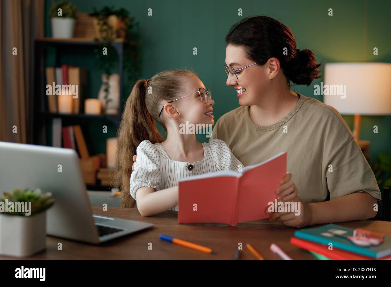 Happy child and adult are sitting at desk. Girl doing homework or ...