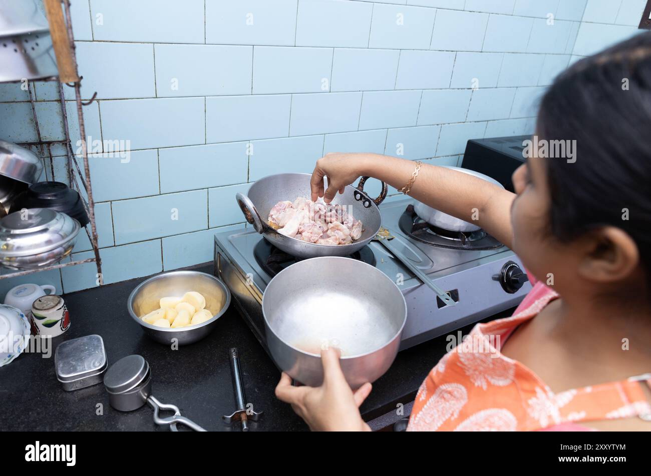 An Indian housewife wearing cooking apron in kitchen making chicken ...