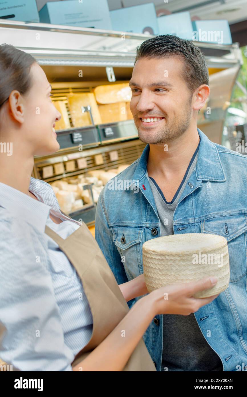 Female shop worker showing large cheese to customer Stock Photo - Alamy