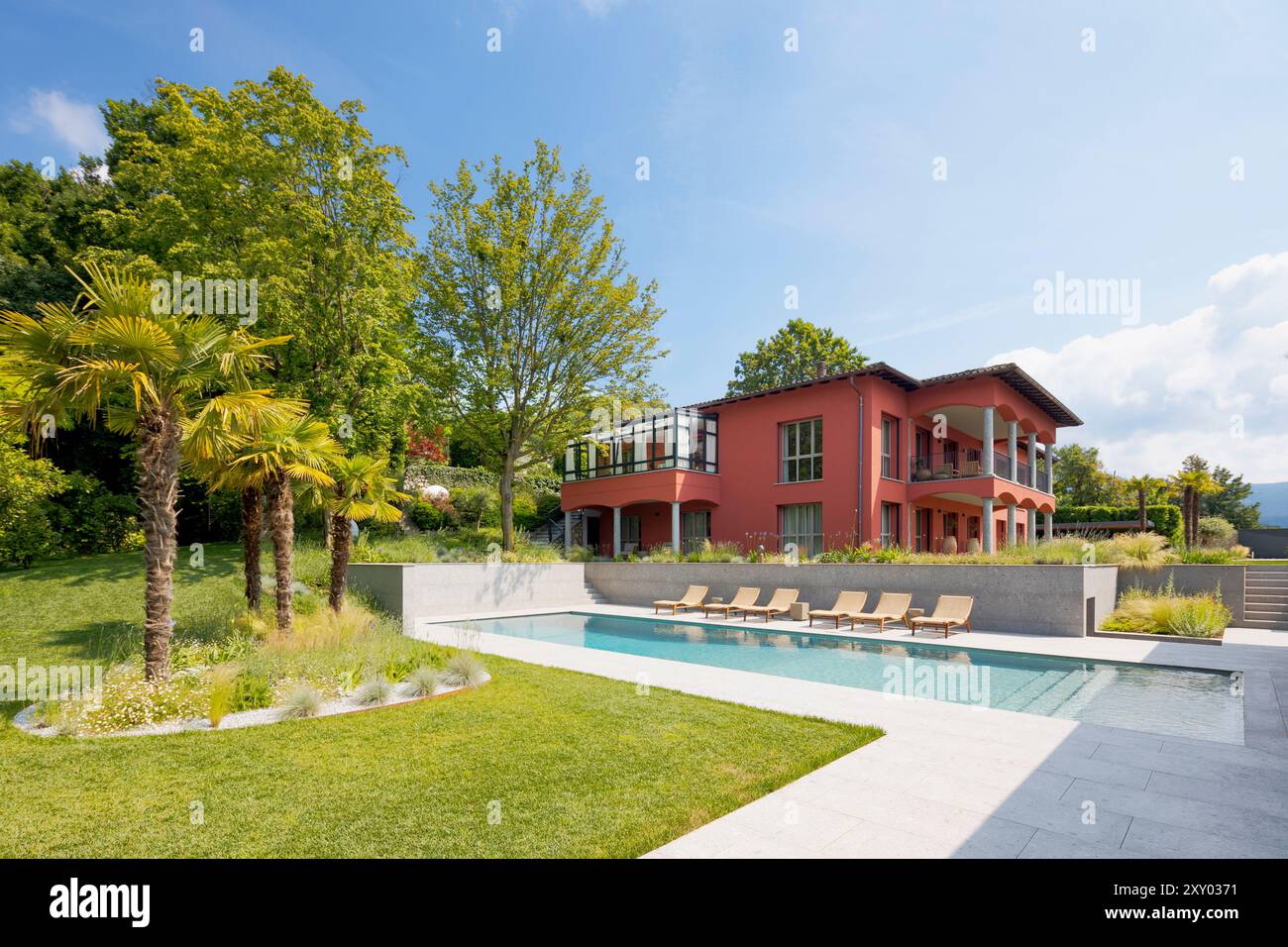 Red-walled villa in a big green garden with trees. There is a big ...