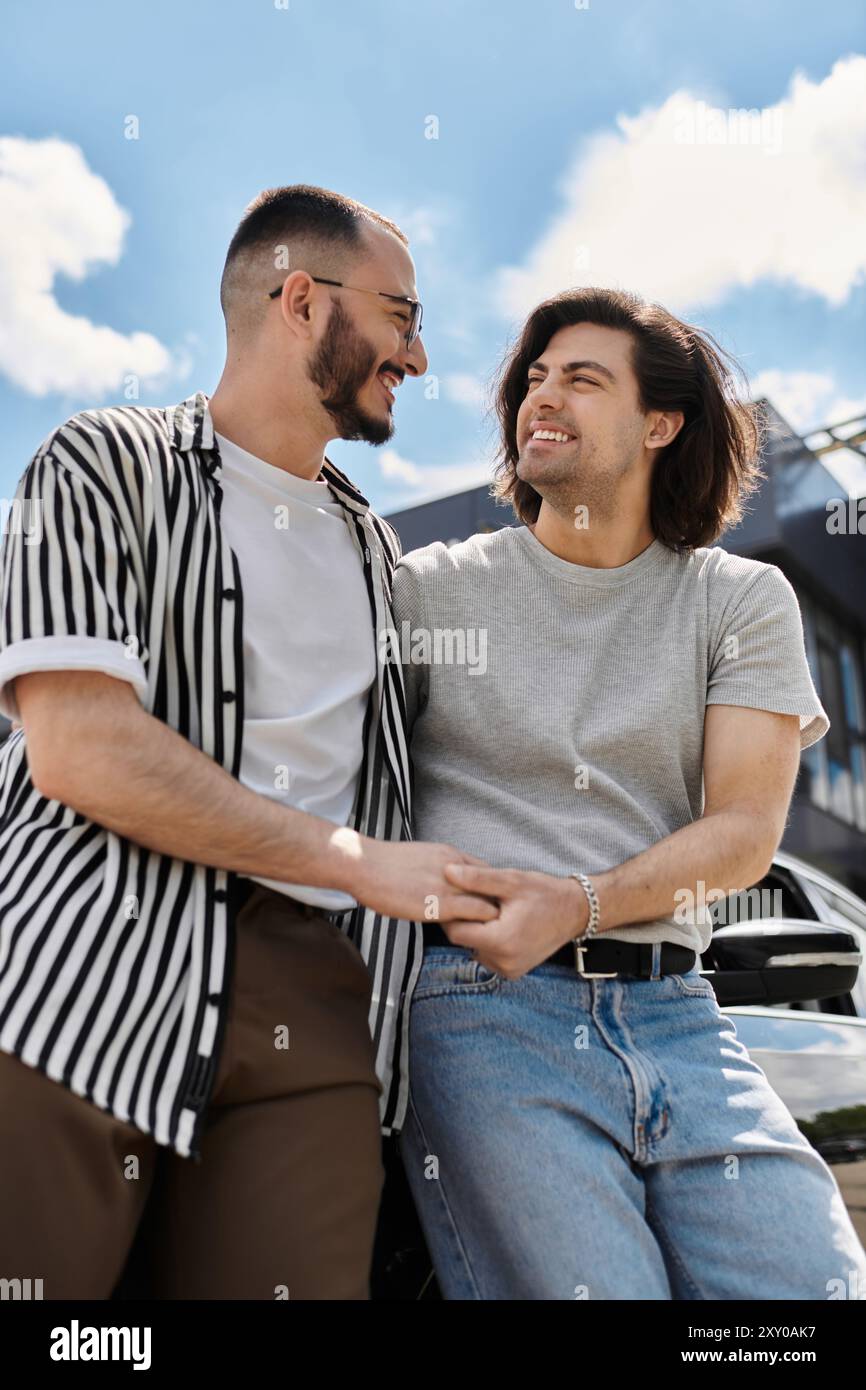 Two men, holding hands, laugh and gaze at each other as they walk ...