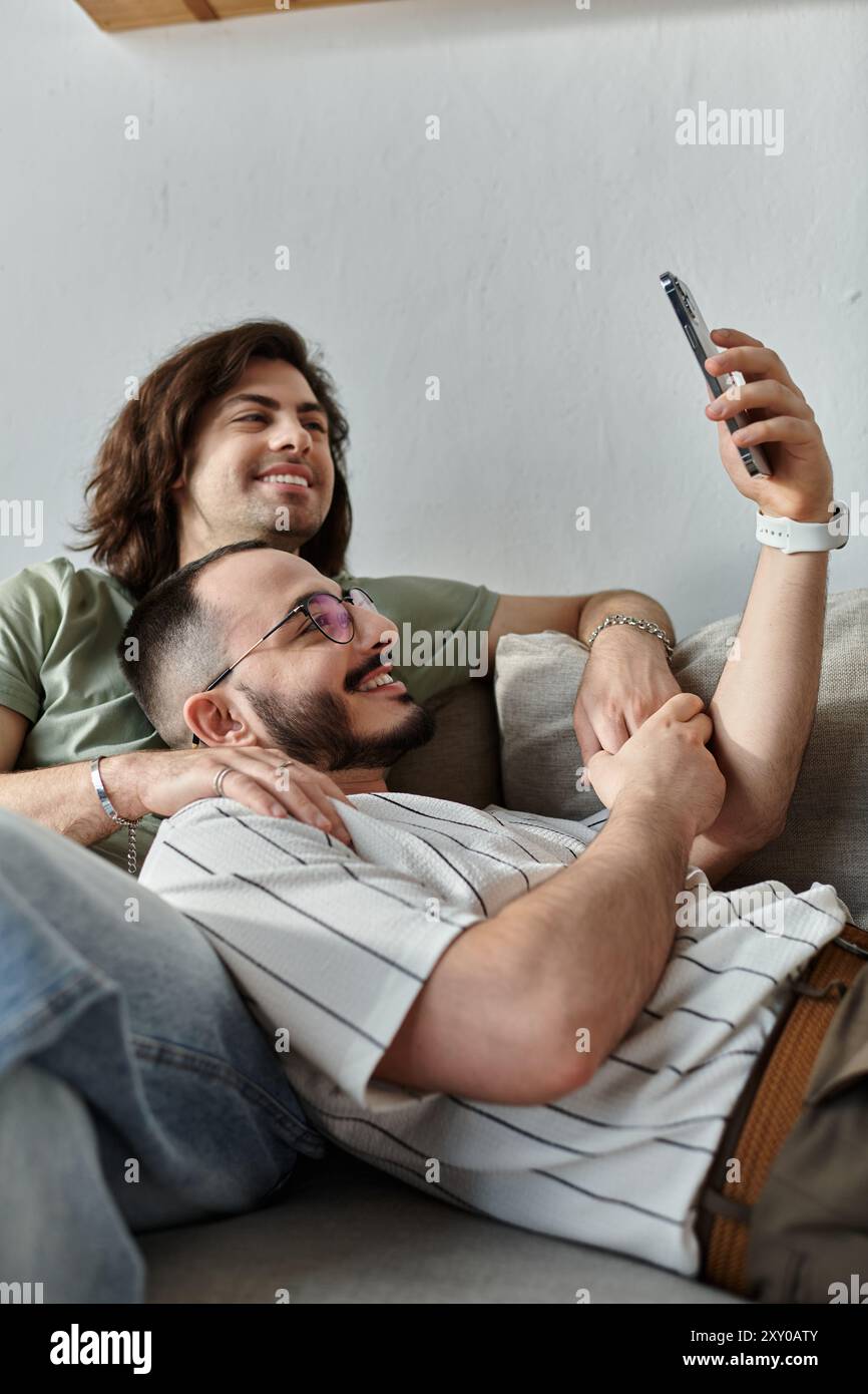 Two men relax on a couch, laughing while looking at a phone screen ...