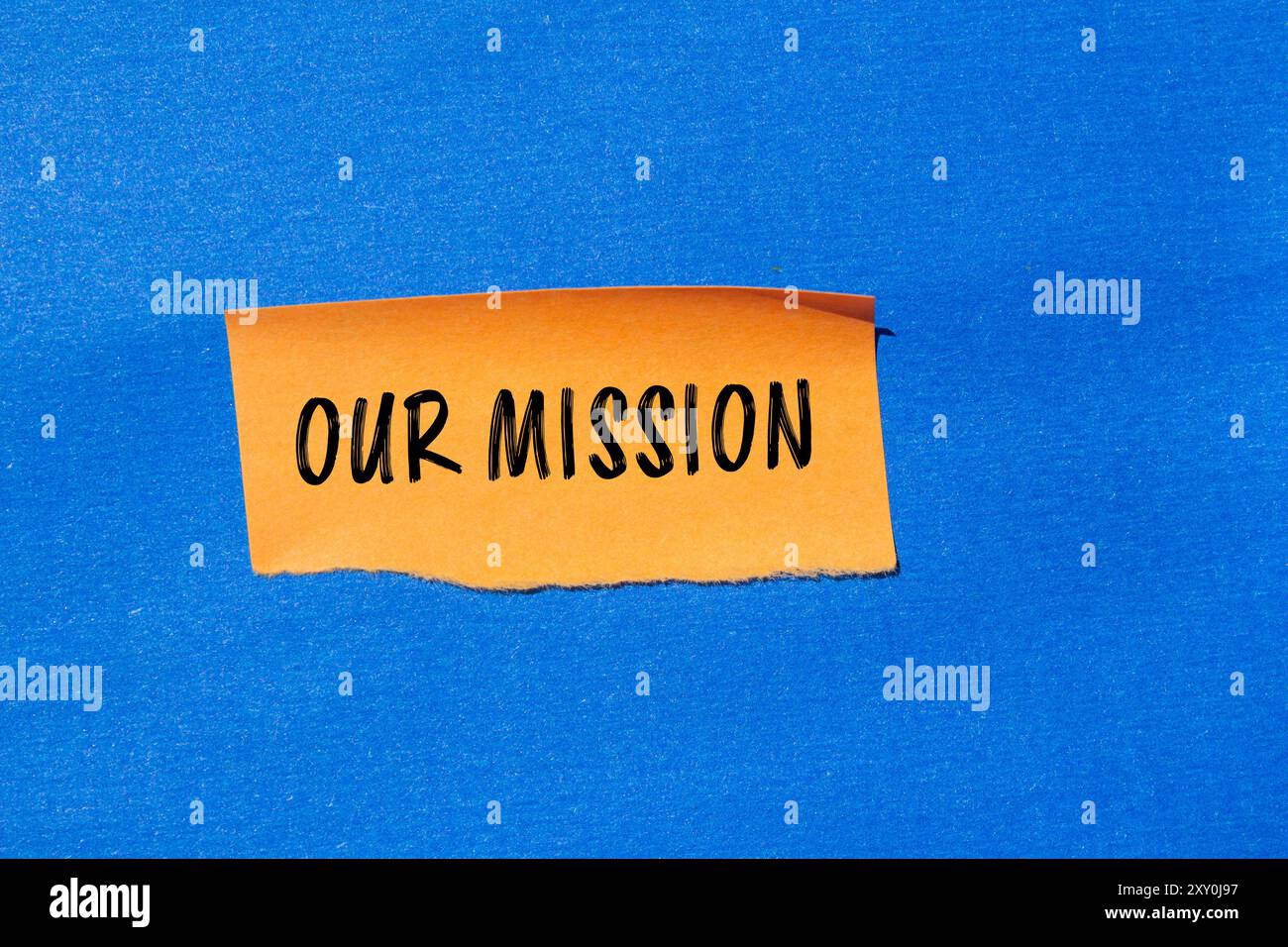 Our mission message written on ripped torn orange paper piece with blue background. Conceptual ...