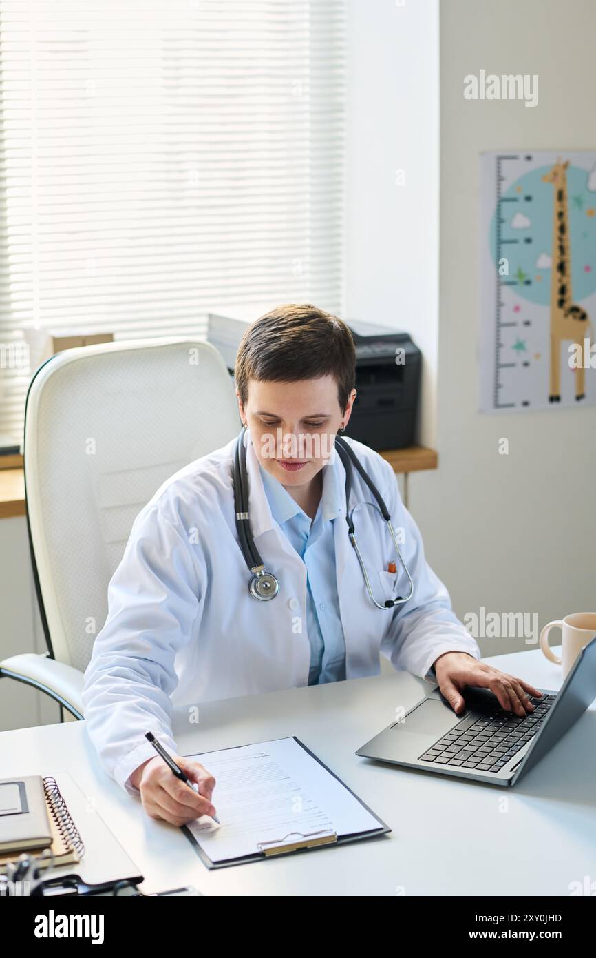 Portrait of a female doctor reviewing patient records while sitting at ...