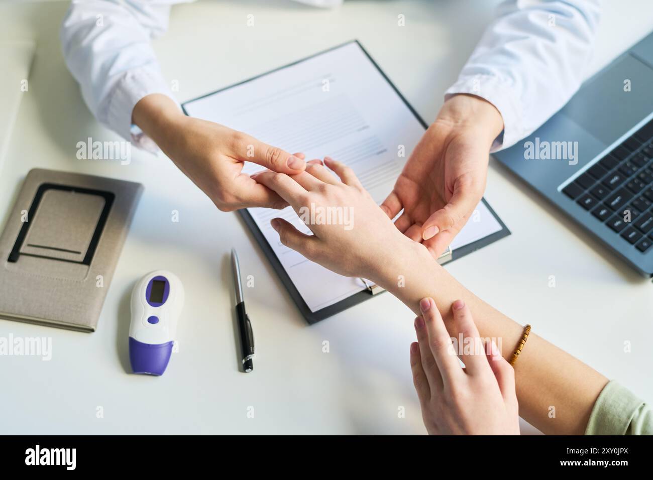 Doctor examining patient's hand while sitting at desk covered with ...