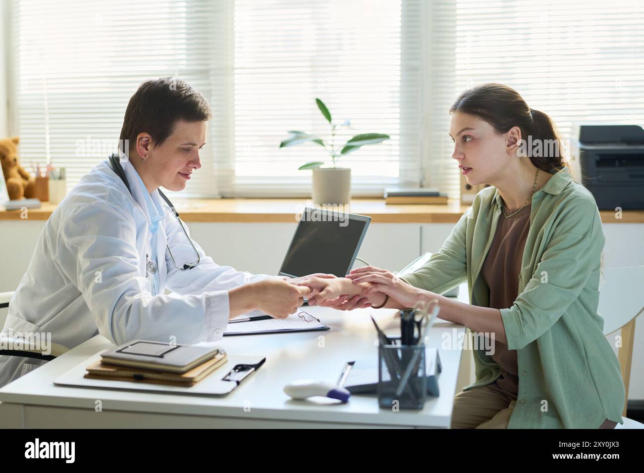 Doctor wearing white coat holding patient's hands during reassuring ...