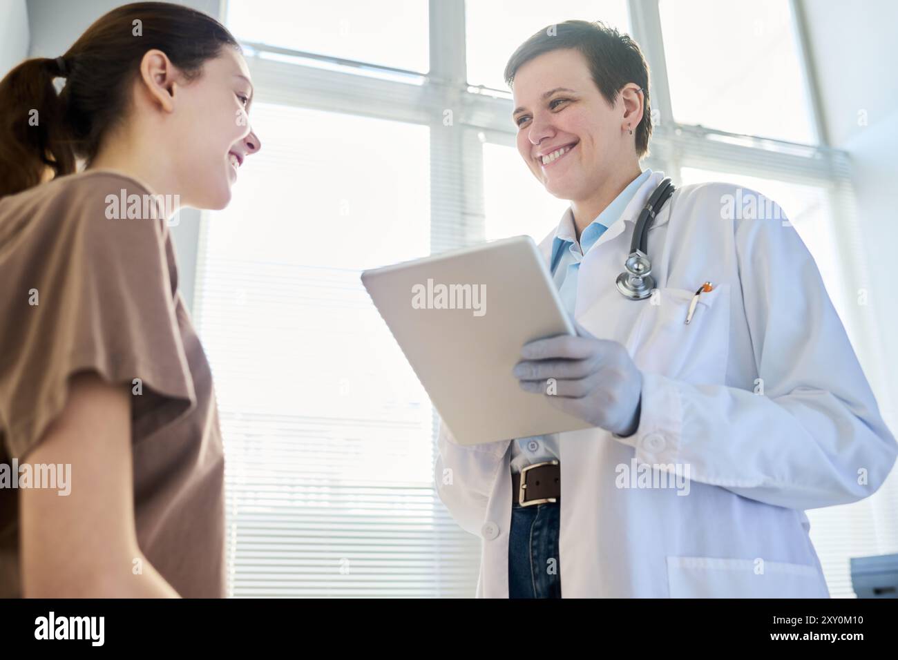 Doctor holding clipboard smiling while conversing with patient in ...