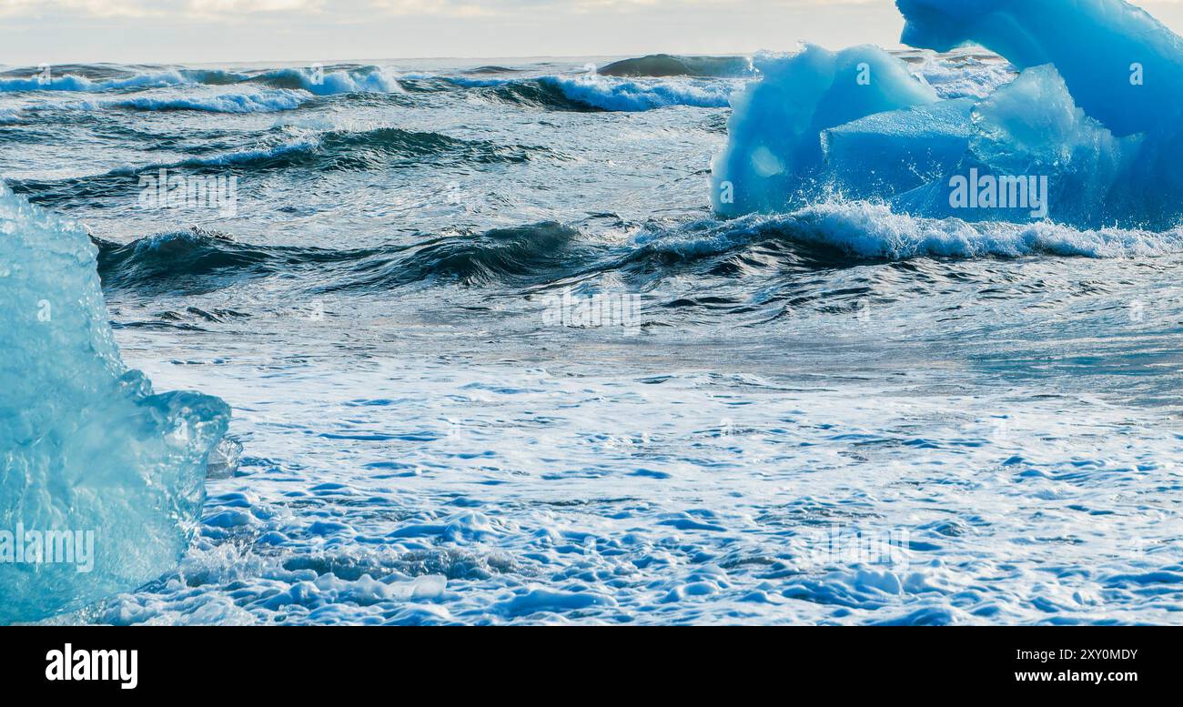 The ocean is calm and blue with a few ice chunks floating on the ...