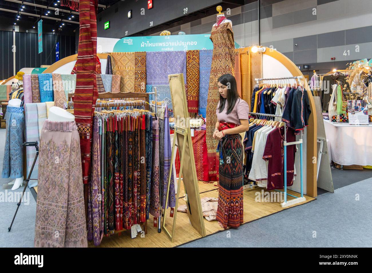 A woman is seen trying on a traditional Thai sarong, at Crafts Bangkok ...
