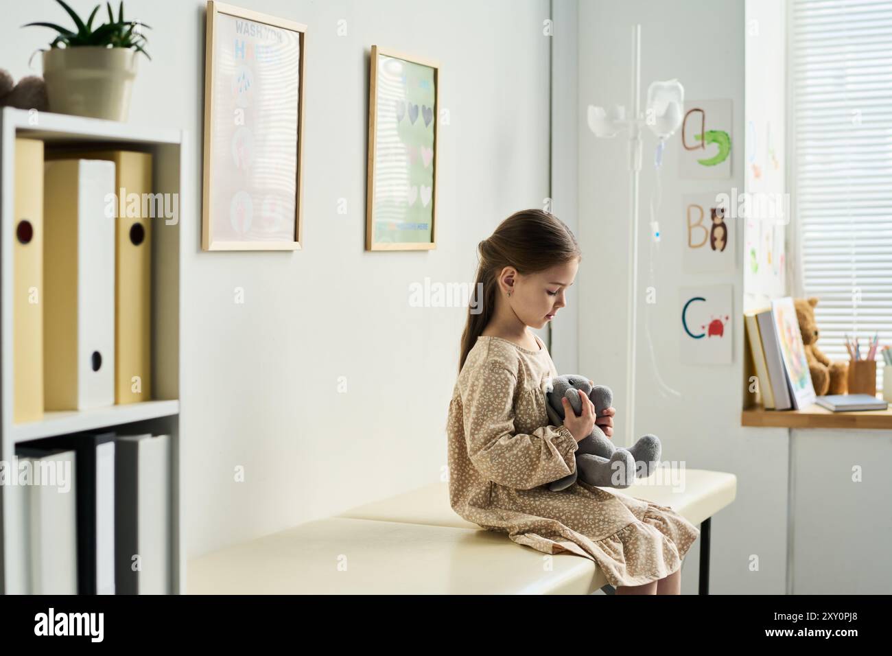 Young girl sitting on bench in pediatric clinic holding stuffed toy ...