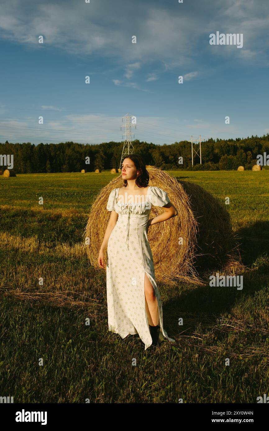 A young woman stands gracefully in a field at sunset, wearing an ...