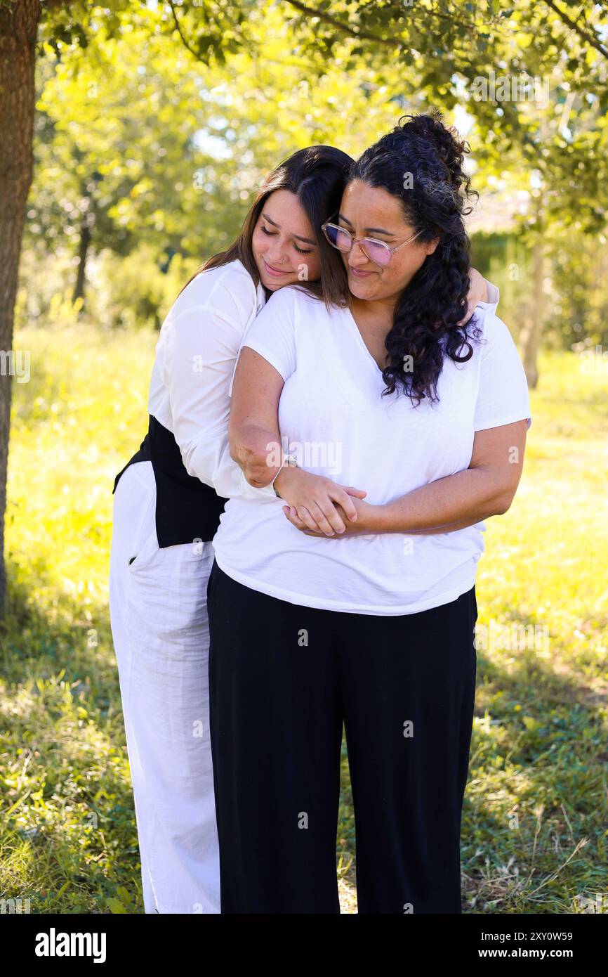 A touching moment as two women embrace in a sunlit park, one with an ...