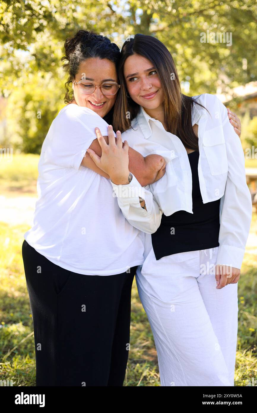 A woman with an arm amputation embraces a young adult in a sunny park ...