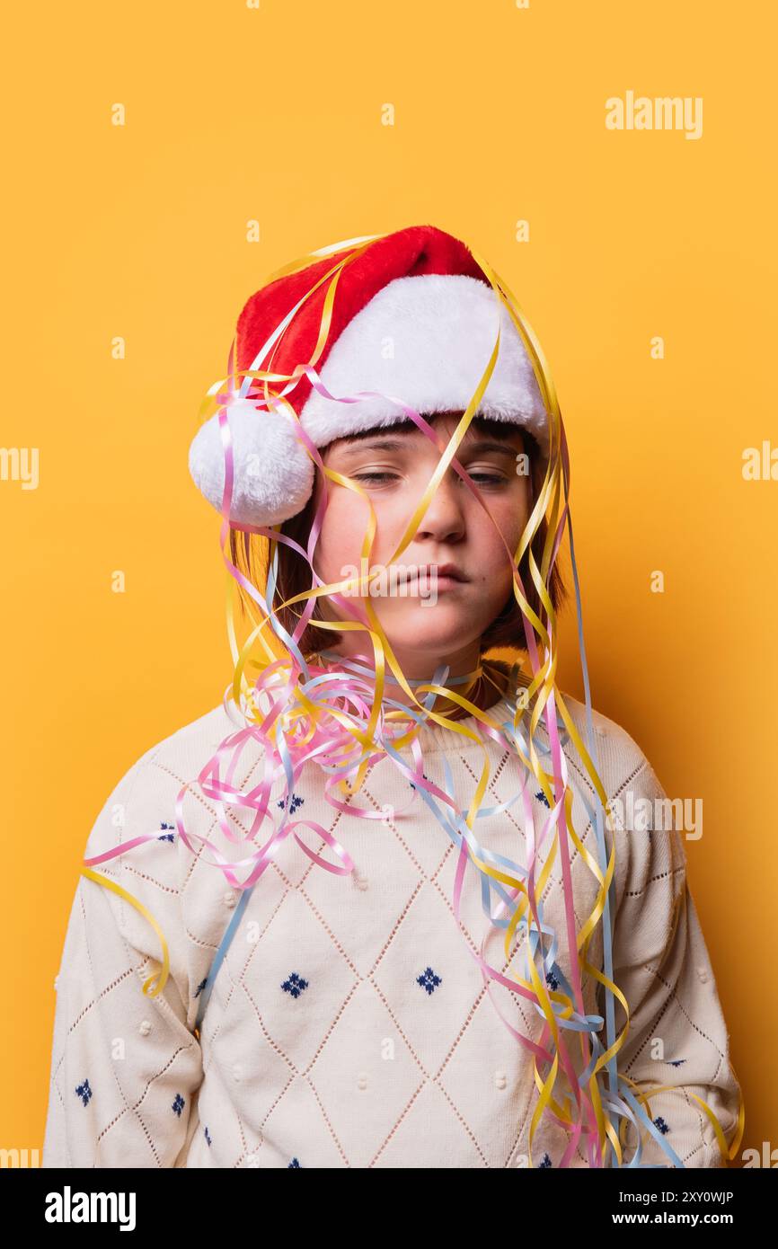 A preteen girl wearing a Santa hat covered in colorful party streamers ...