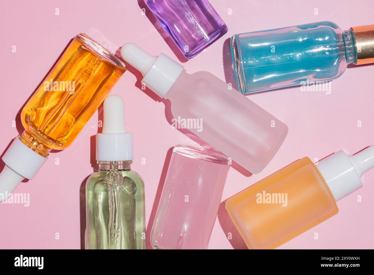 Top view of vibrant serum dropper bottles scattered across a pastel ...