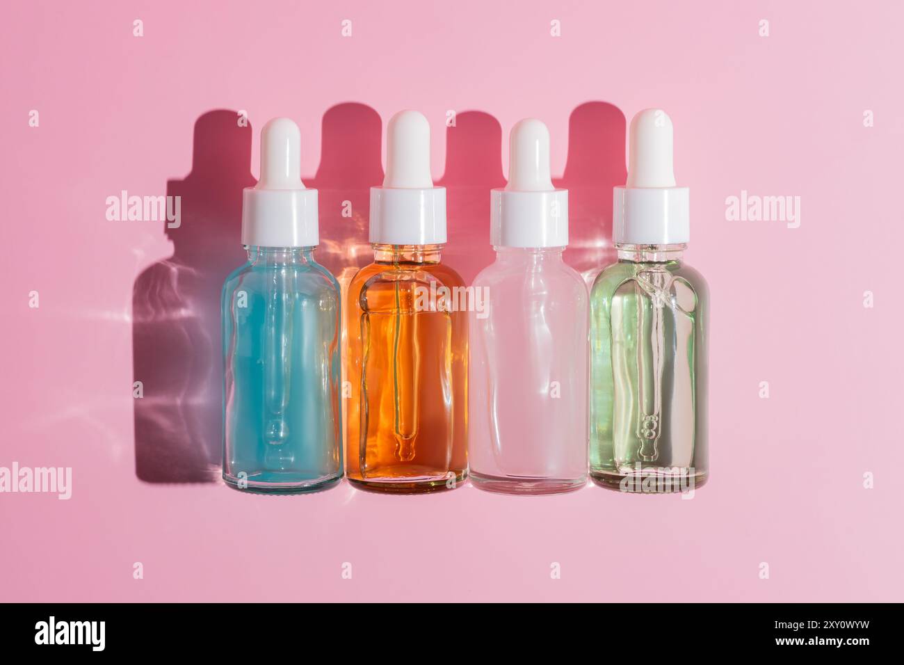 Top view of four colorful serum dropper bottles aligned on a pastel ...
