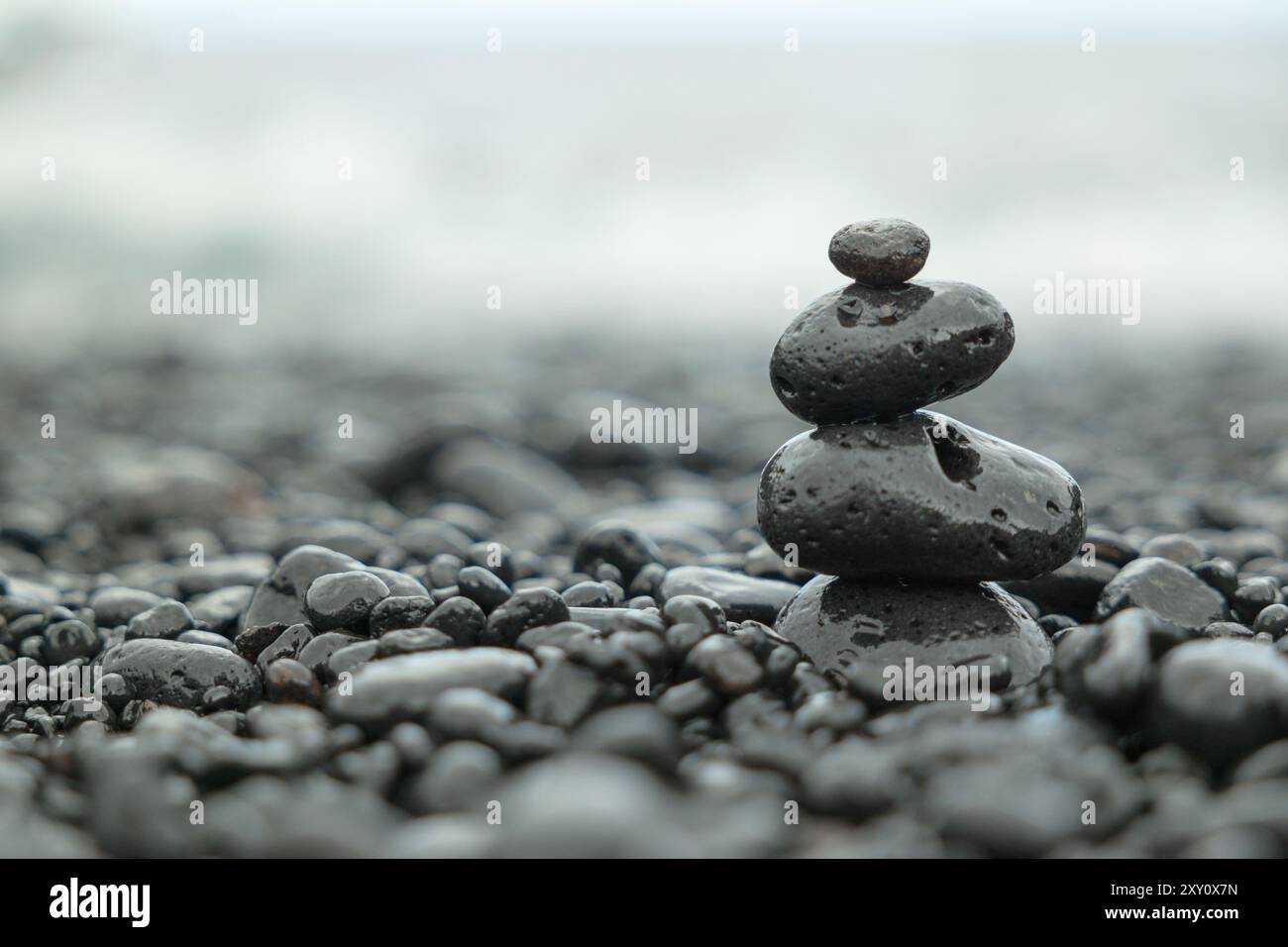 Three wet, black stones stacked in balance on a misty beach with smooth ...