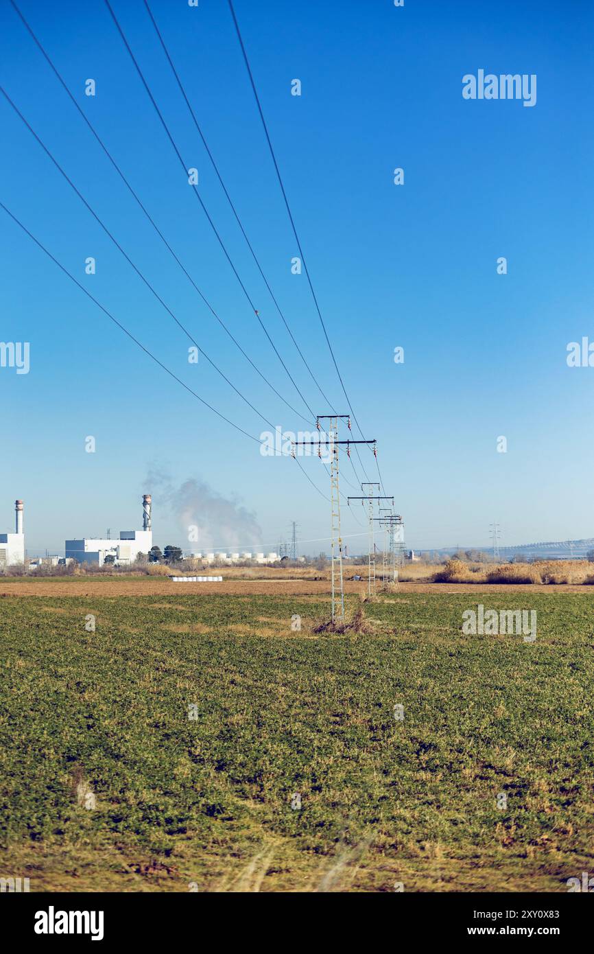Power lines stretching across a field towards an industrial power plant ...