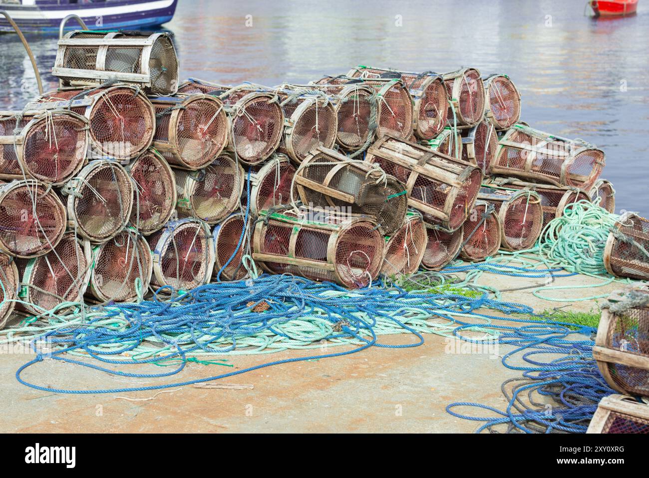 A stack of cylindrical fishing traps, some encased in nets, alongside ...