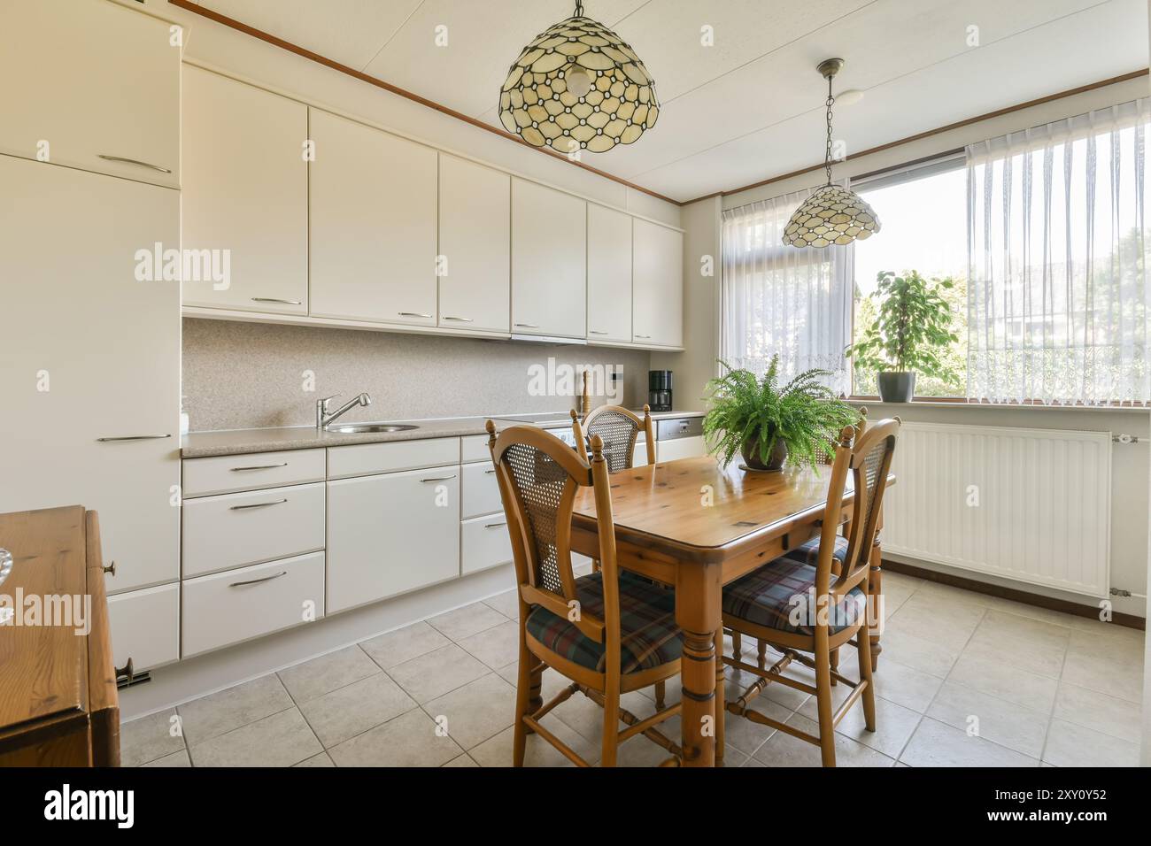 A well-lit kitchen with modern white cabinetry and a wooden dining ...