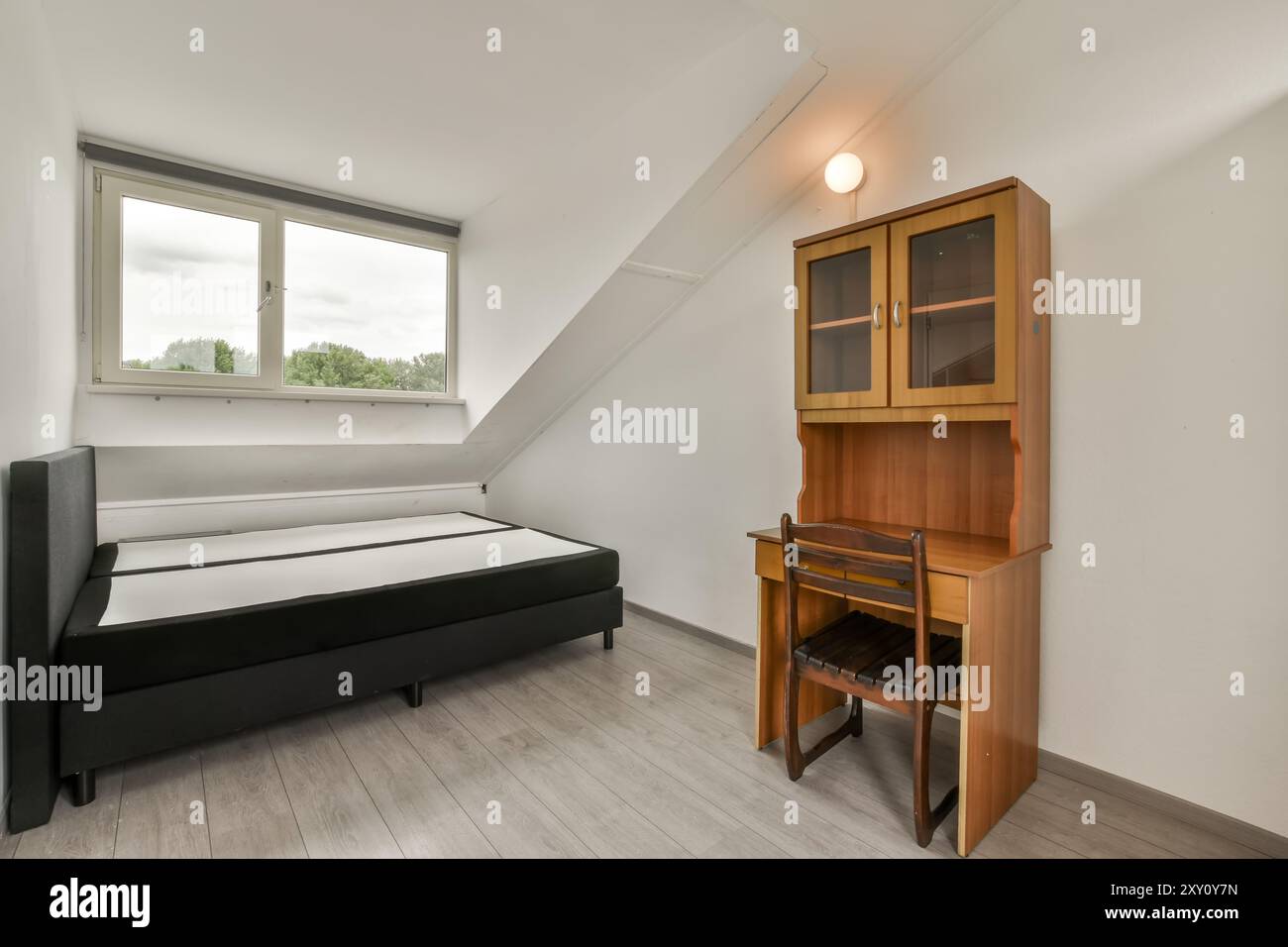 Sparse attic bedroom featuring a modern sofa bed, wooden desk, and ...