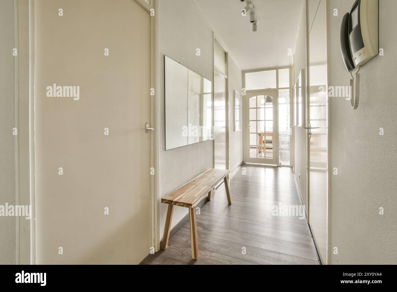 A sunny and minimalist corridor featuring a simple wooden bench, large ...