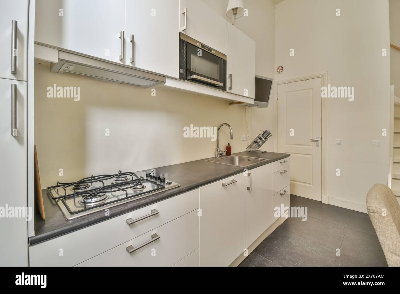 A sleek modern kitchen with white cabinetry, stainless steel gas stove ...