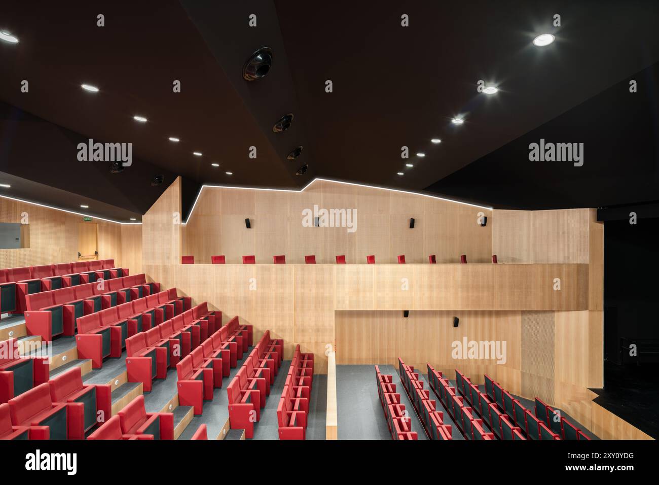 A spacious, contemporary auditorium featuring rows of red seats and ...