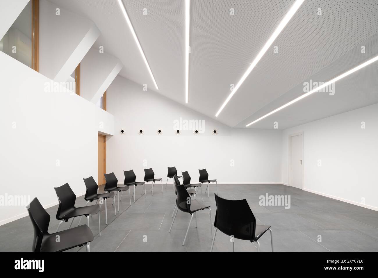 Sleek auditorium interior featuring rows of black chairs, white walls ...